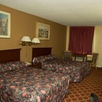 Quarto de hotel com duas camas, uma escrivaninha, duas luminárias e cortina vermelha.