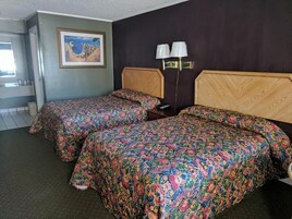Quarto de hotel com duas camas, um quadro na parede e uma mesa de cabeceira com luminárias.