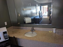 Casa de banho com lavatório, espelho, micro-ondas e televisão ao fundo.