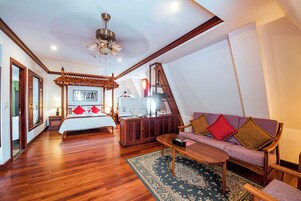 Quarto com cama, piso de madeira, ventilador de teto e sofá com almofadas.