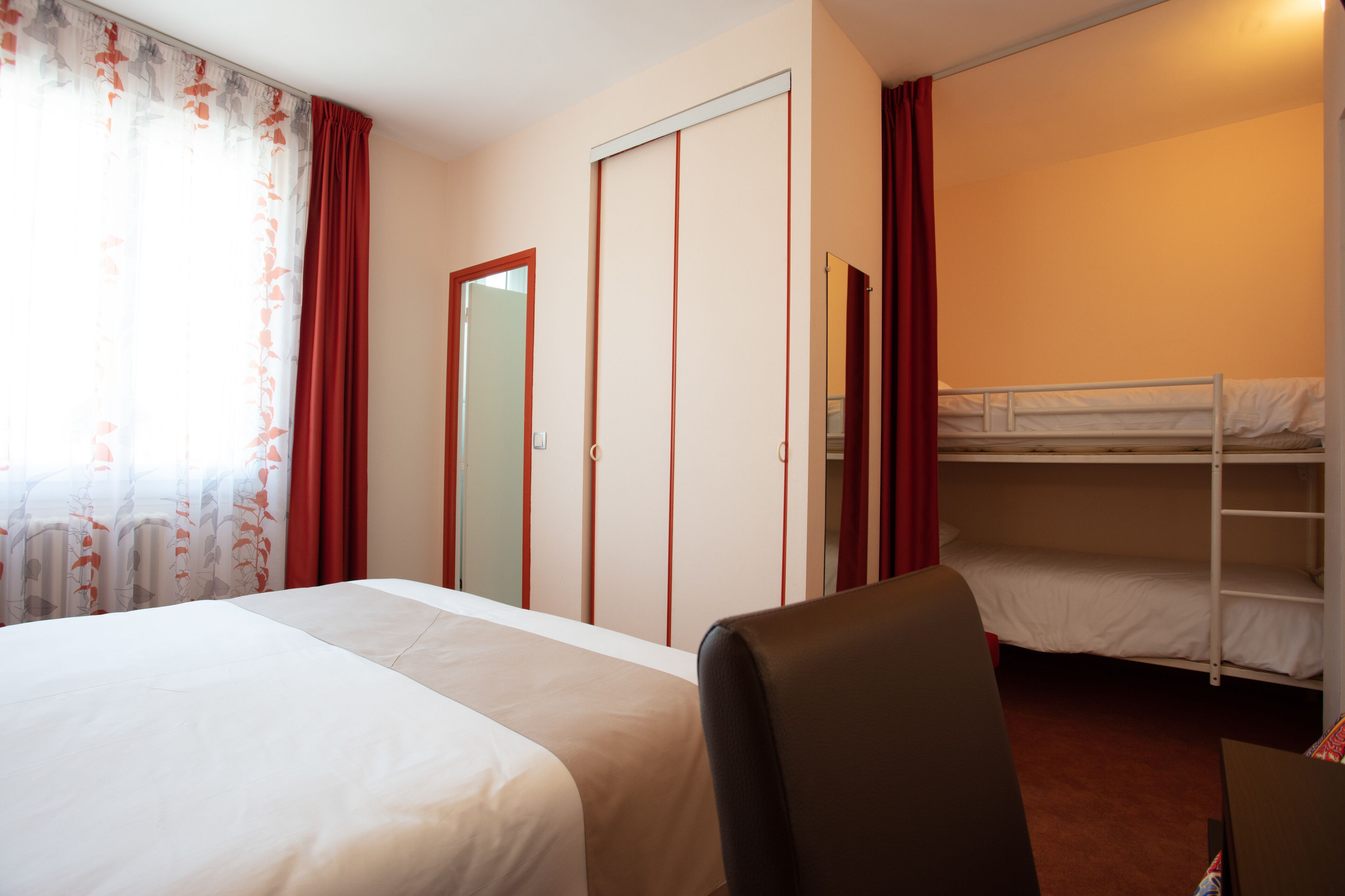 Quarto de hotel com cama, cadeira, guarda-roupa e beliche.