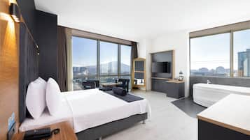 Quarto de hotel moderno com uma cama grande, uma escrivaninha, um sofá, uma TV e uma banheira.