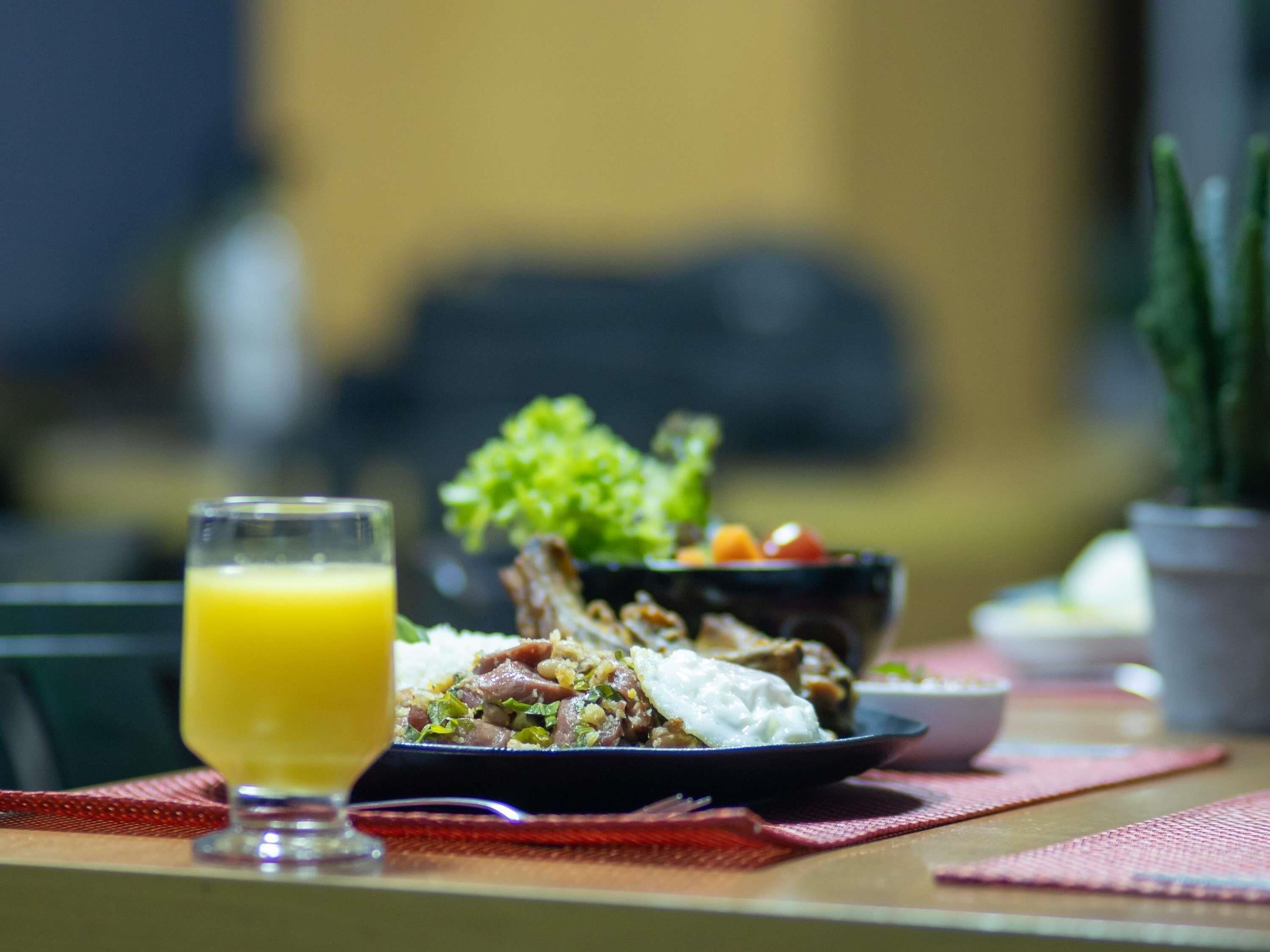 Uma mesa de jantar com um prato de comida, um copo de suco de laranja e uma pequena tigela.