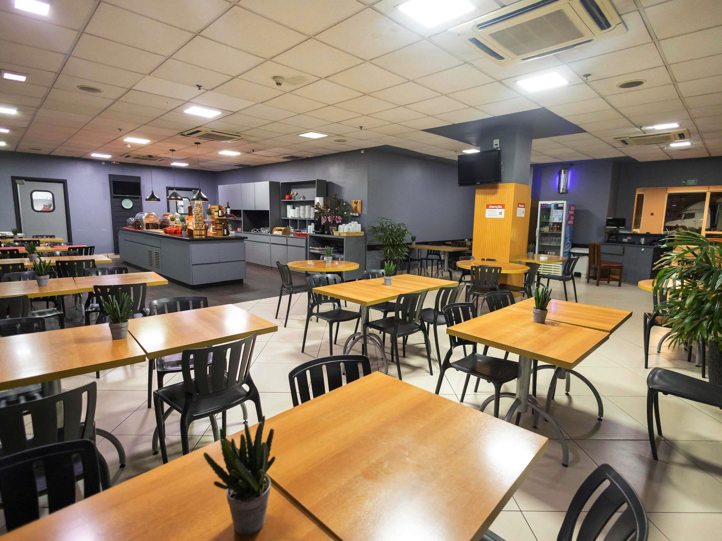 Um restaurante amplo com várias mesas e cadeiras, uma área de cozinha e um balcão com menu.
