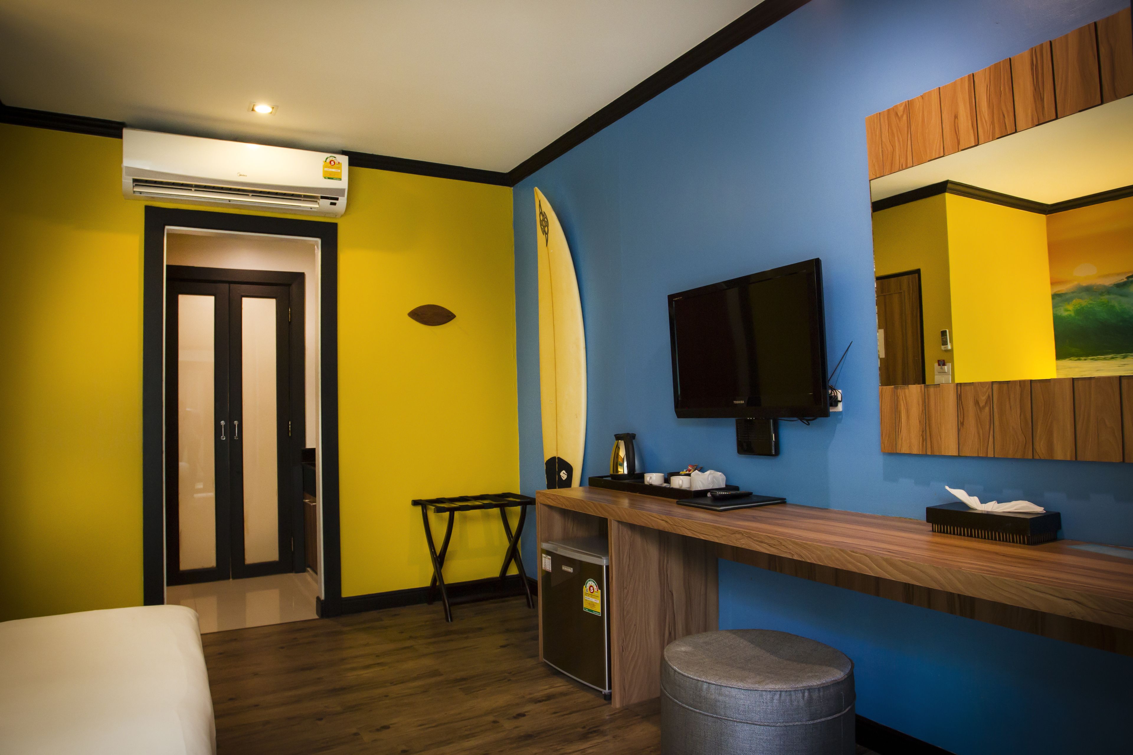 Quarto com cama, escrivaninha, televisão e ar condicionado.