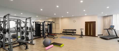 Uma academia com diversos equipamentos de exercício, esteira e um espelho grande na parede.