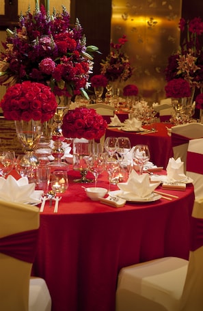 Mesa posta para um evento formal, com toalhas vermelhas, guardanapos brancos e centros de mesa florais.