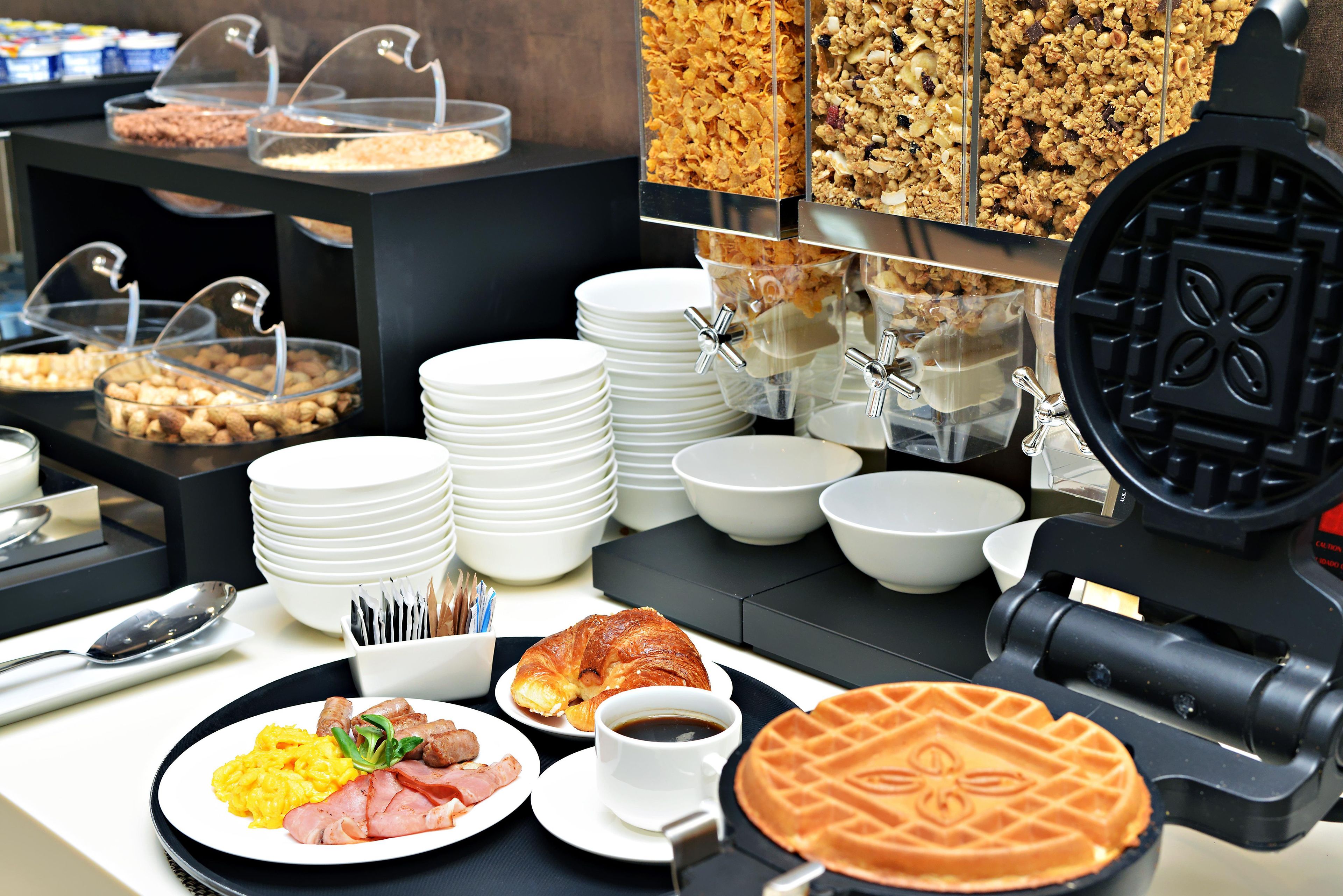 Buffet com diversos alimentos, incluindo cereais, doces e waffles.