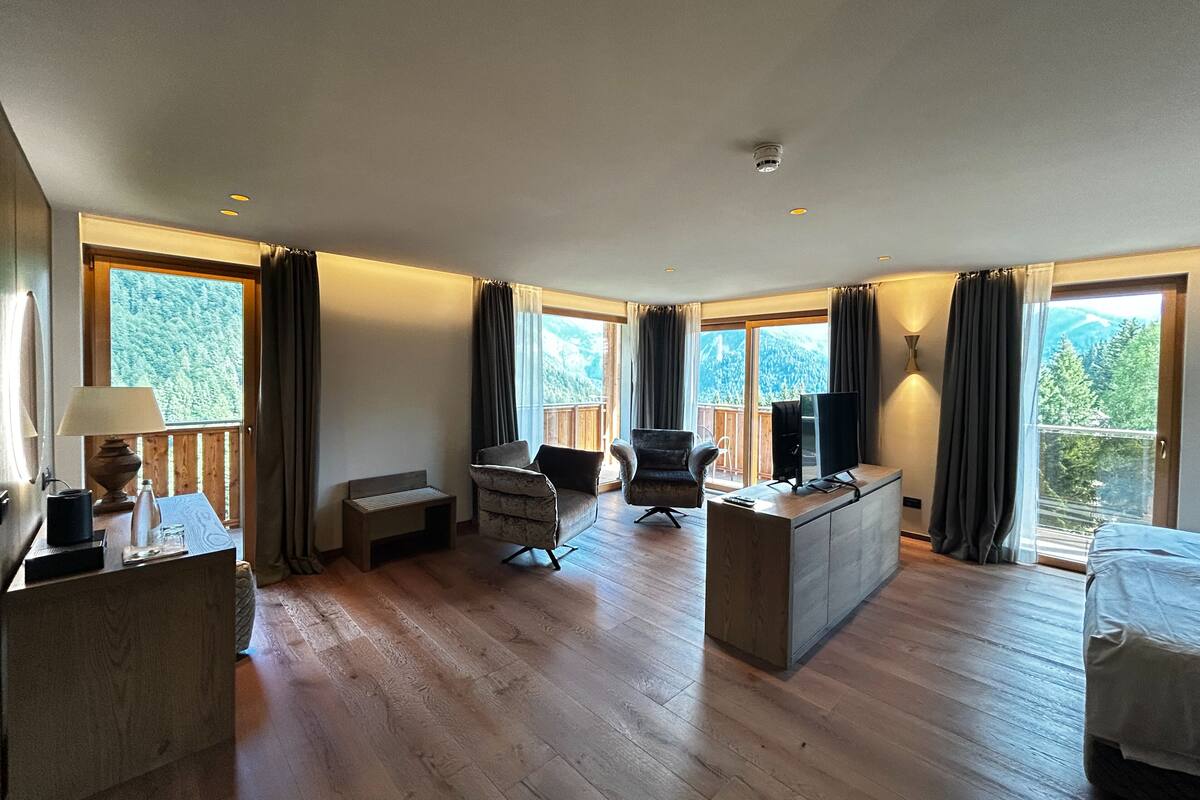 Um quarto espaçoso com piso de madeira, um sofá, uma poltrona, uma TV e uma cama.