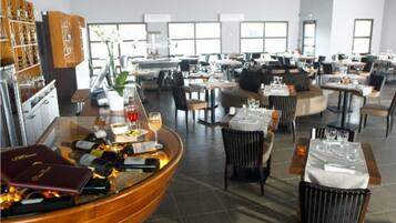 Um restaurante espaçoso com pé-direito alto, amplas janelas e diferentes opções de assentos, incluindo mesas e cadeiras.