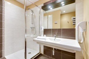 Uma casa de banho moderna com chuveiro envolto em vidro, lavatório branco e secador de cabelo.