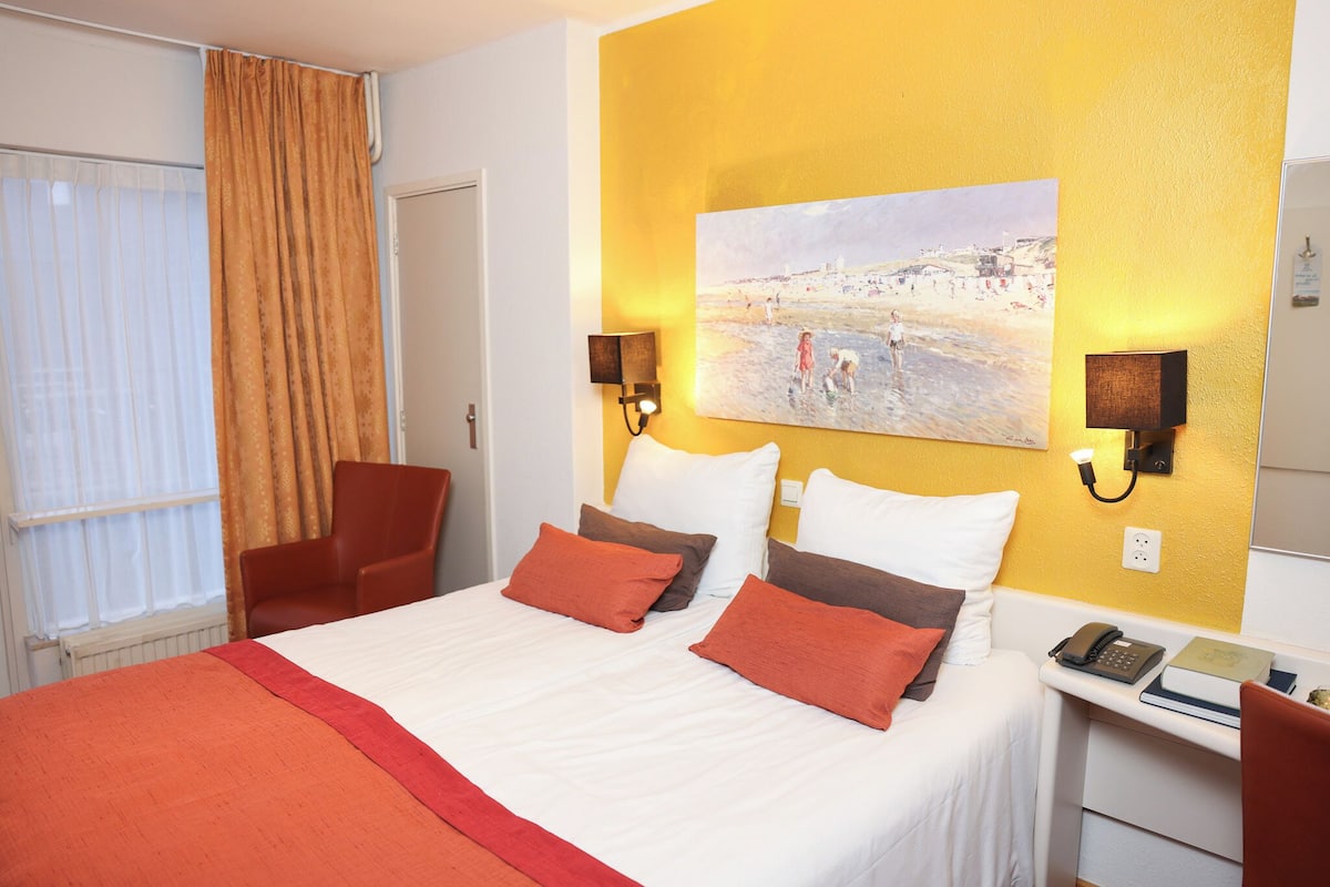 Quarto de hotel com cama, cadeira, quadro e escrivaninha com telefone.