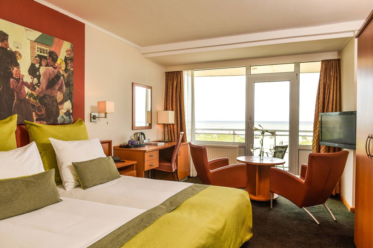 Quarto de hotel com cama, escrivaninha, cadeiras, televisão e uma grande janela com vista.