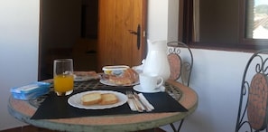 Uma mesa de café da manhã com pão, um copo de suco de laranja, uma xícara, uma chaleira e um prato de croissants.