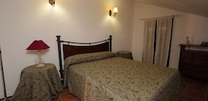 Quarto com cama, mesa de cabeceira, luminária e cômoda.