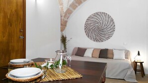 Uma área de jantar com uma mesa de madeira posta para dois, uma peça decorativa na parede e um arco de pedra.