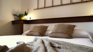 Uma cama bem arrumada com duas almofadas e um cobertor, uma luminária de cabeceira e uma prateleira na parede com uma planta e uma luminária.