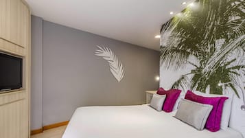 Quarto com cama, TV, decoração em formato de folha na parede e um mural de palmeira.