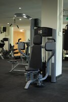 Uma academia com máquinas de exercício, um espelho fixado na parede e uma porta ao fundo.