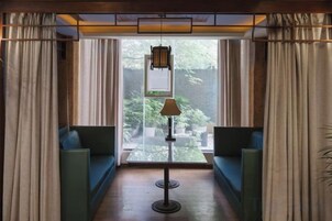 Quarto com sofá, mesa com abajur e vista pela janela.