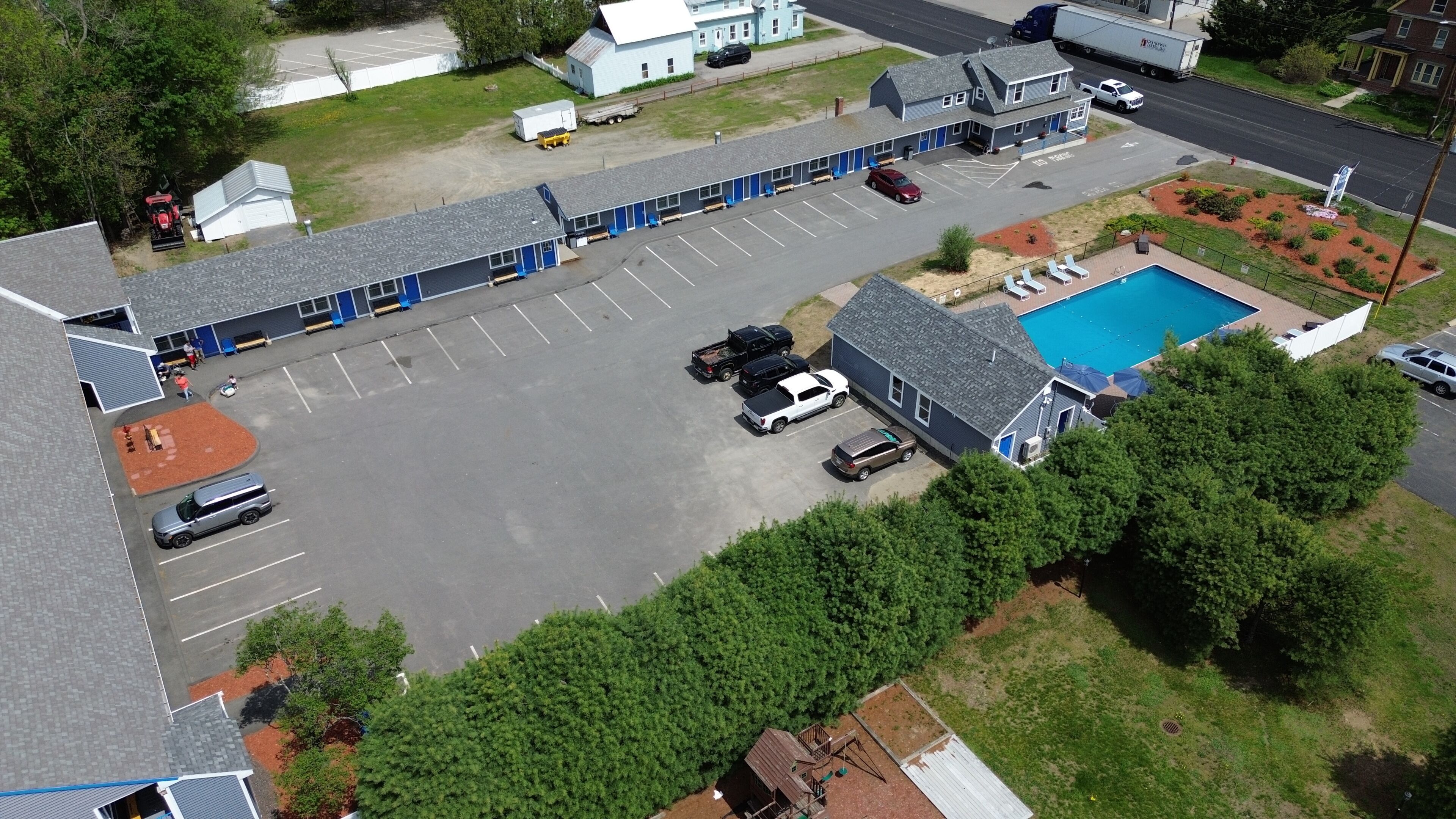 Vista aérea de um motel com piscina, estacionamento e um pequeno prédio ao lado da piscina.
