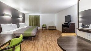 Quarto de hotel com cama, escrivaninha, cadeira, televisão e espelho.