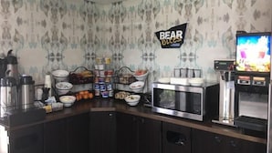 Uma cozinha compacta com micro-ondas, cafeteira e geladeira. Há diversos recipientes de alimentos e uma placa com a inscrição 'BEAR Bites'.