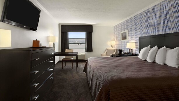 Quarto de hotel com cama, escrivaninha, cadeira, televisão e janela com vista.