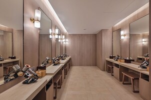 Um banheiro moderno com várias pias, espelhos e secadores de cabelo.