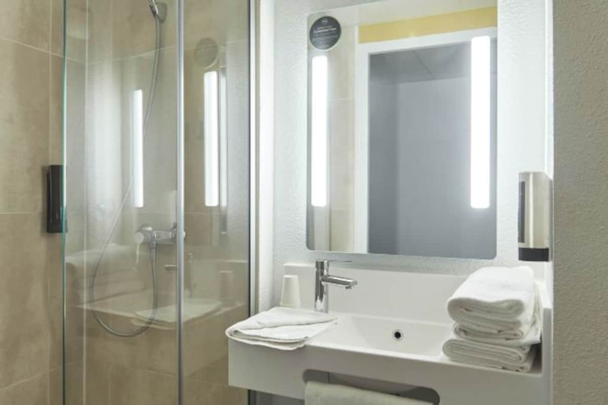 Uma casa de banho moderna com cabine de duche em vidro, lavatório branco com espelho e toalhas bem arrumadas.