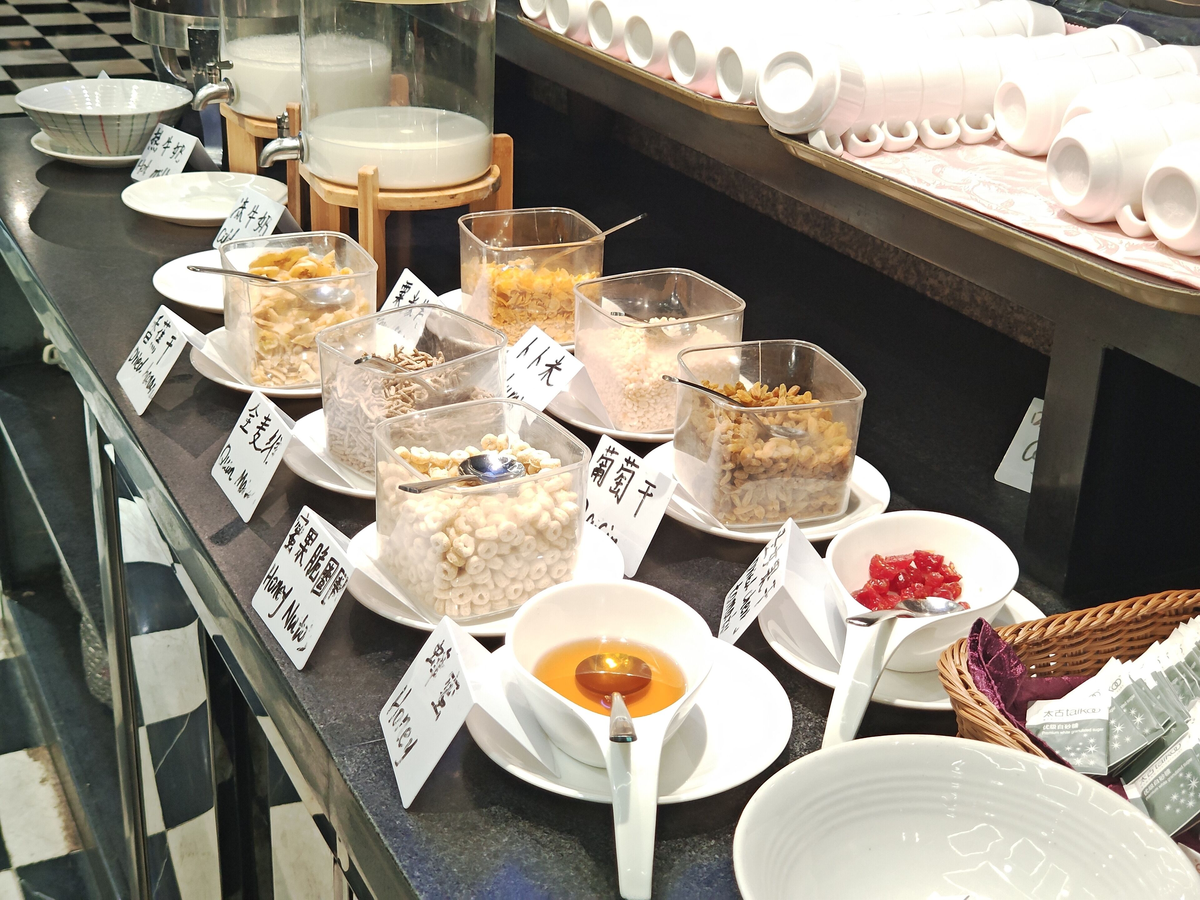 Buffet com diversos alimentos e pratos, incluindo cereais, arroz e uma tigela de sopa.
