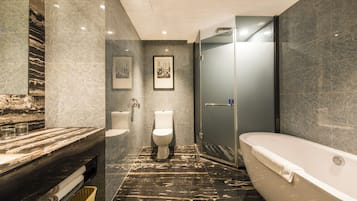 Uma casa de banho moderna com soalho em mármore, banheira, sanita e espelho sobre a toucador.