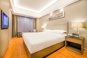 Quarto de hotel com cama grande, abajures, televisão de tela plana e uma obra de arte emoldurada na parede.