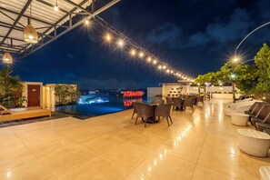 Terraço ao ar livre com piscina, área de estar e luzes de corda.