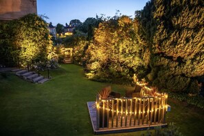 Uma área de jardim bem iluminada com um deck de madeira, rodeada por vegetação exuberante e árvores.