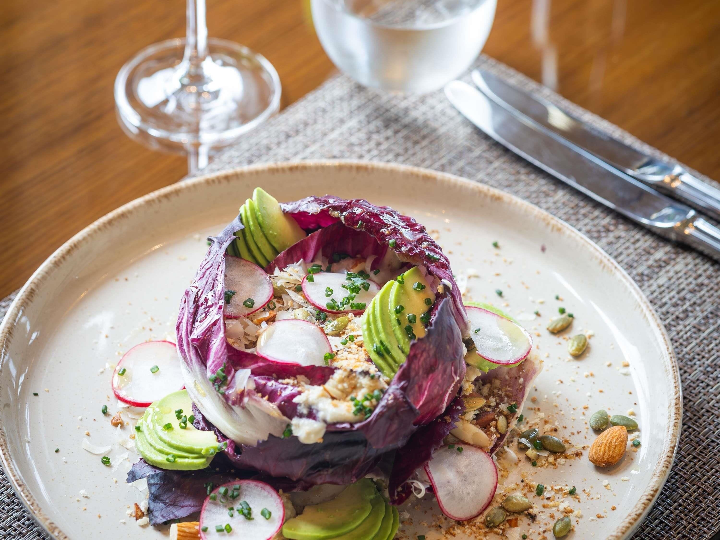 Prato de comida com salada, um copo de água e talheres sobre a mesa.