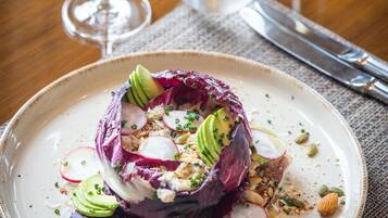 Prato de comida com salada, um copo de água e talheres sobre a mesa.