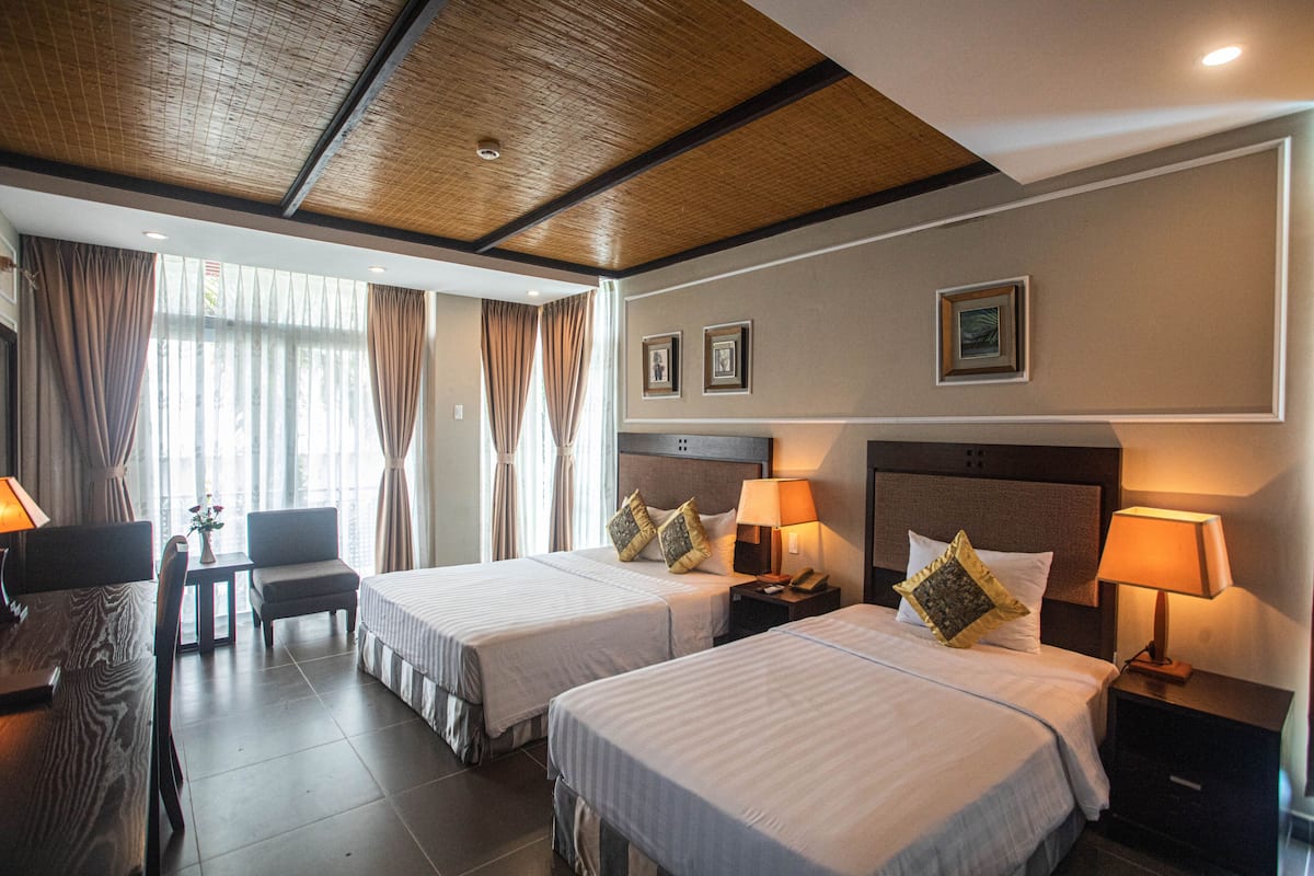 Quarto de hotel com duas camas, uma escrivaninha, uma cadeira e uma mesa de cabeceira com luminárias.