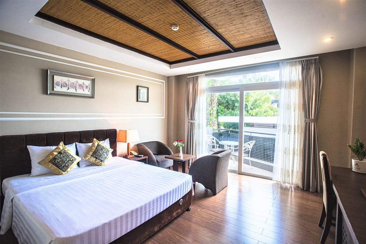 Quarto de hotel com uma cama grande, uma mesa de escritório, uma cadeira e varanda com vista para o verde.