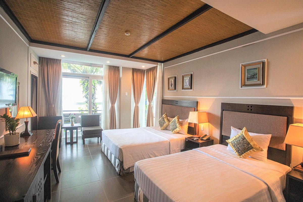 Quarto de hotel com duas camas, uma escrivaninha, uma cadeira e uma mesa de jantar.