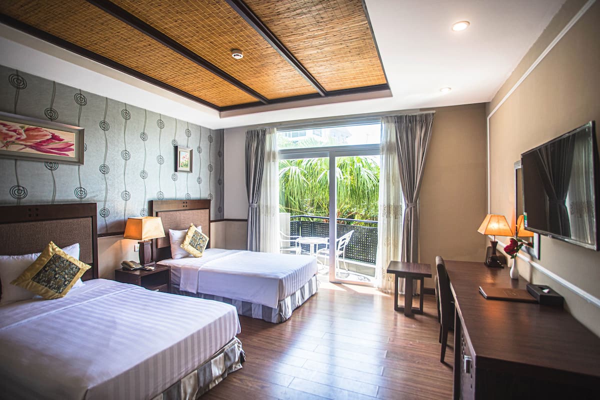 Quarto de hotel com duas camas, televisão, varanda com vista para vegetação e teto de madeira.