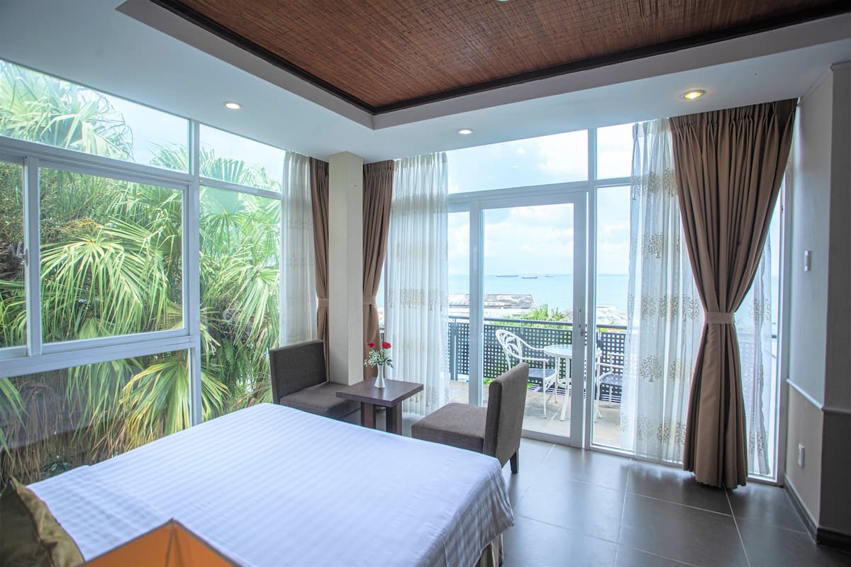 Quarto de hotel com uma cama grande, uma mesa pequena, uma cadeira e uma varanda com vista para o mar.