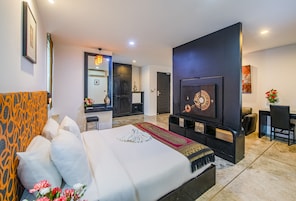 Quarto de hotel moderno com uma cama grande, televisão de tela plana na parede, escrivaninha com cadeira e um pequeno espaço de estar com sofá e poltronas.