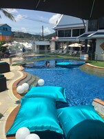 Uma área de piscina com espreguiçadeiras e guarda-sóis, cercada por edifícios e um céu claro.