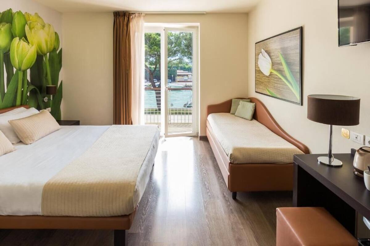 Quarto de hotel com duas camas, uma escrivaninha, uma cadeira, televisão e varanda com vista para o exterior.