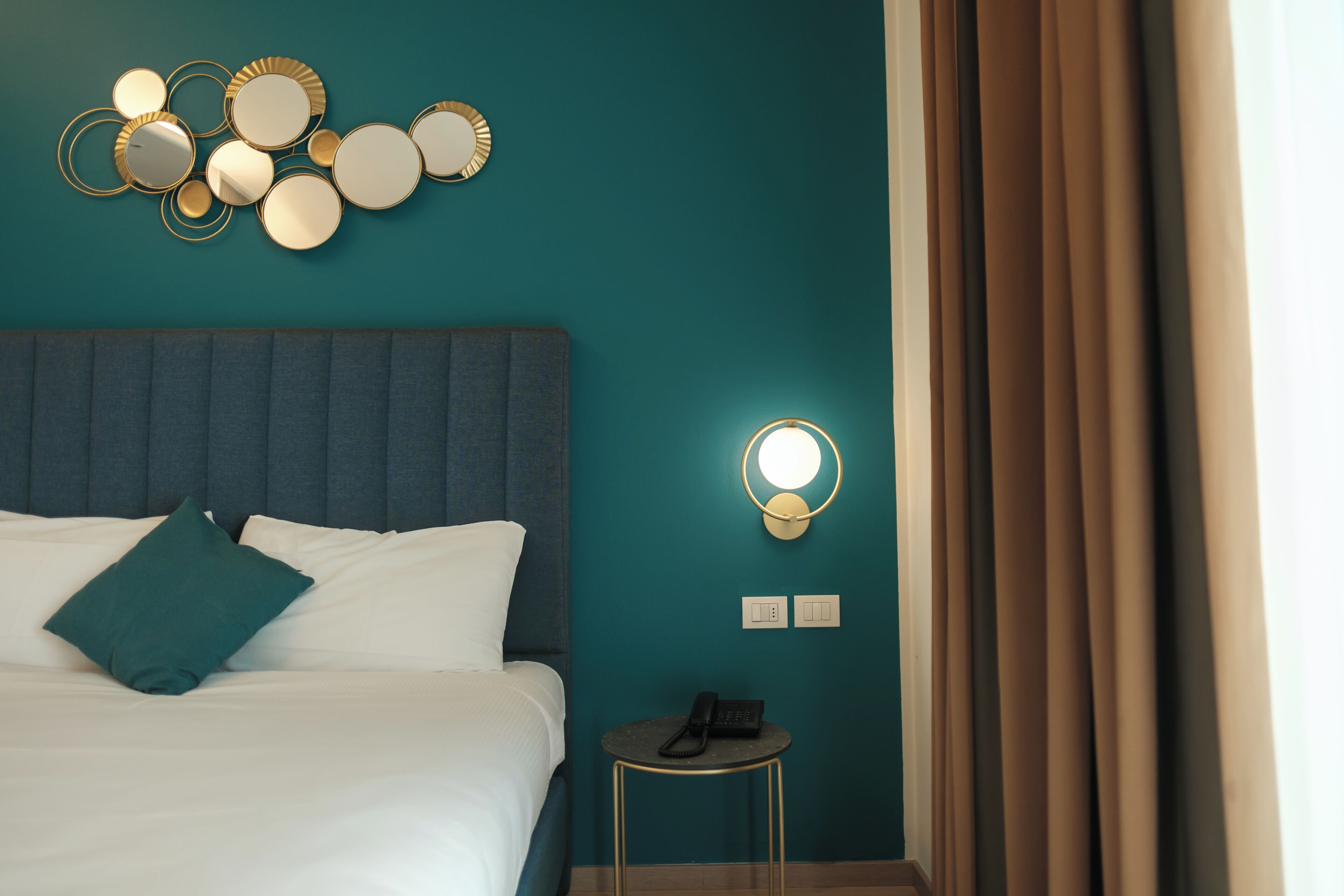 Quarto de hotel com cama, luminária na parede, telefone e tomada.