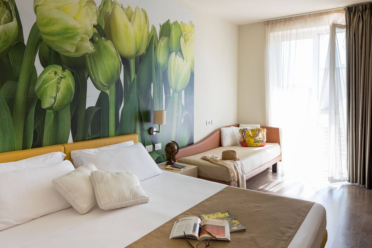 Quarto de hotel com uma cama grande, uma cama menor, uma mesinha de cabeceira e uma pintura de tulipas na parede.