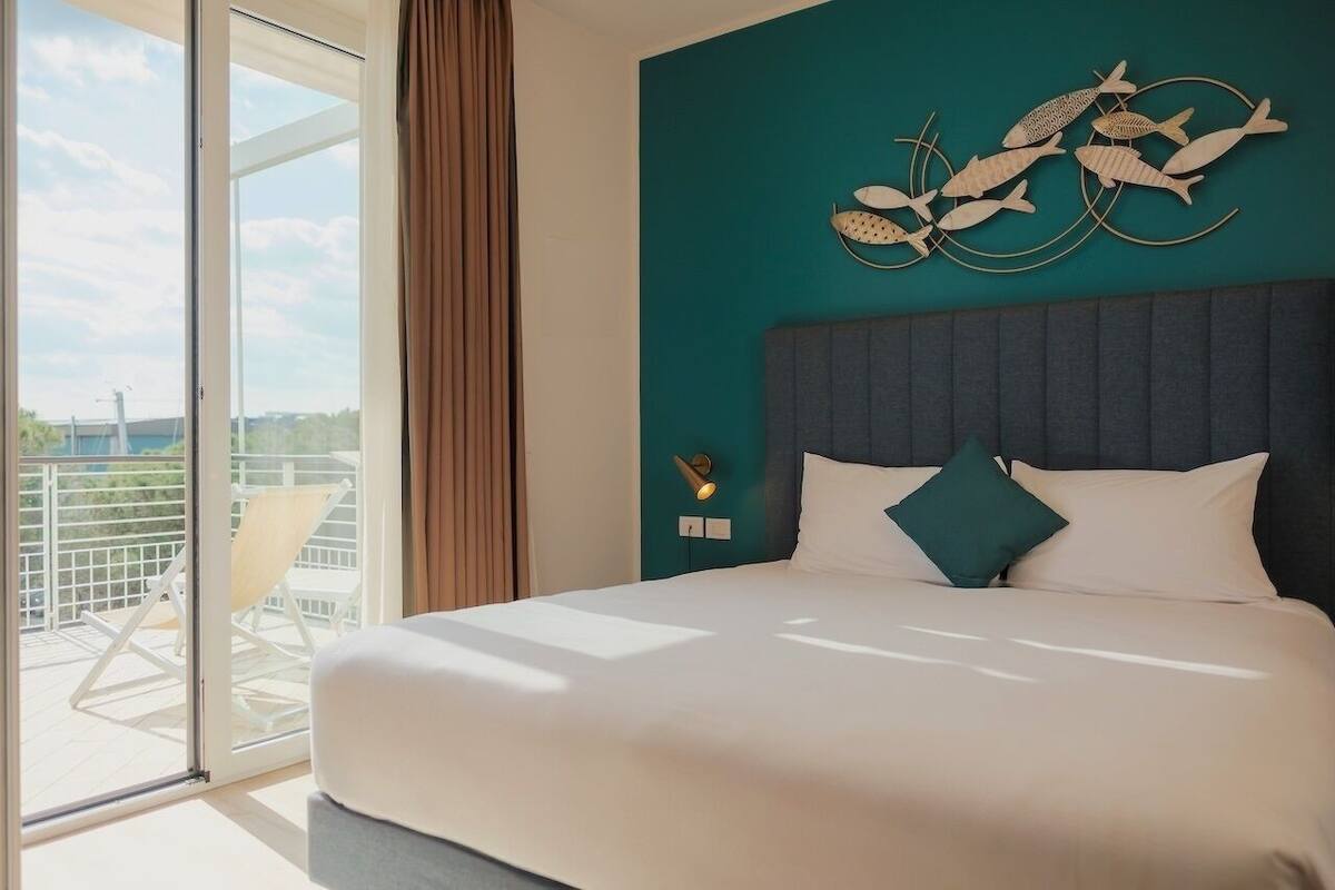 Quarto de hotel com uma cama, decoração de peixe na parede, uma varanda com cadeira e vista para o exterior.