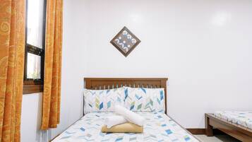 Quarto com cama de madeira, janela com cortinas, luminária fixada na parede e um pequeno objeto decorativo.