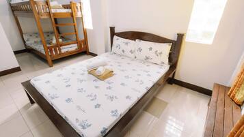 Quarto com uma cama de solteiro, uma cama beliche de madeira e uma mesinha.